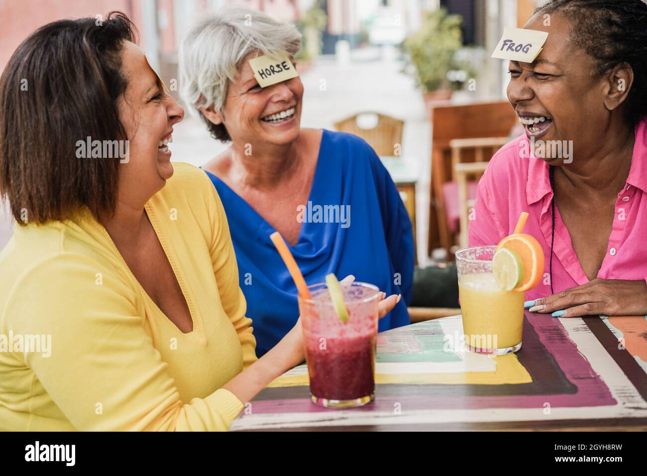 Multiracial senior women having fun playing guessing forehead game at ...