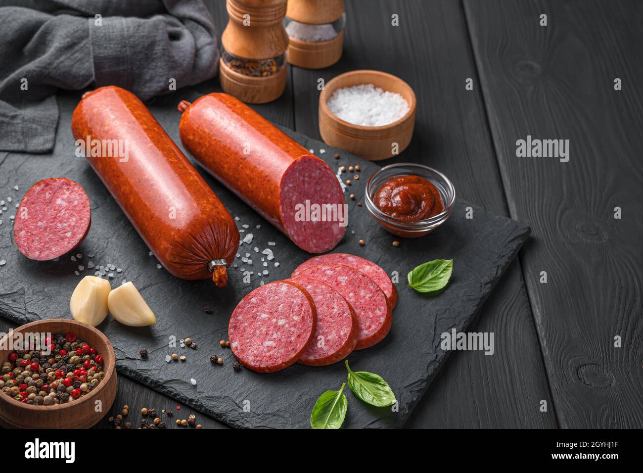 Smoked sausage on a dark background with garlic, spices and basil. Side ...