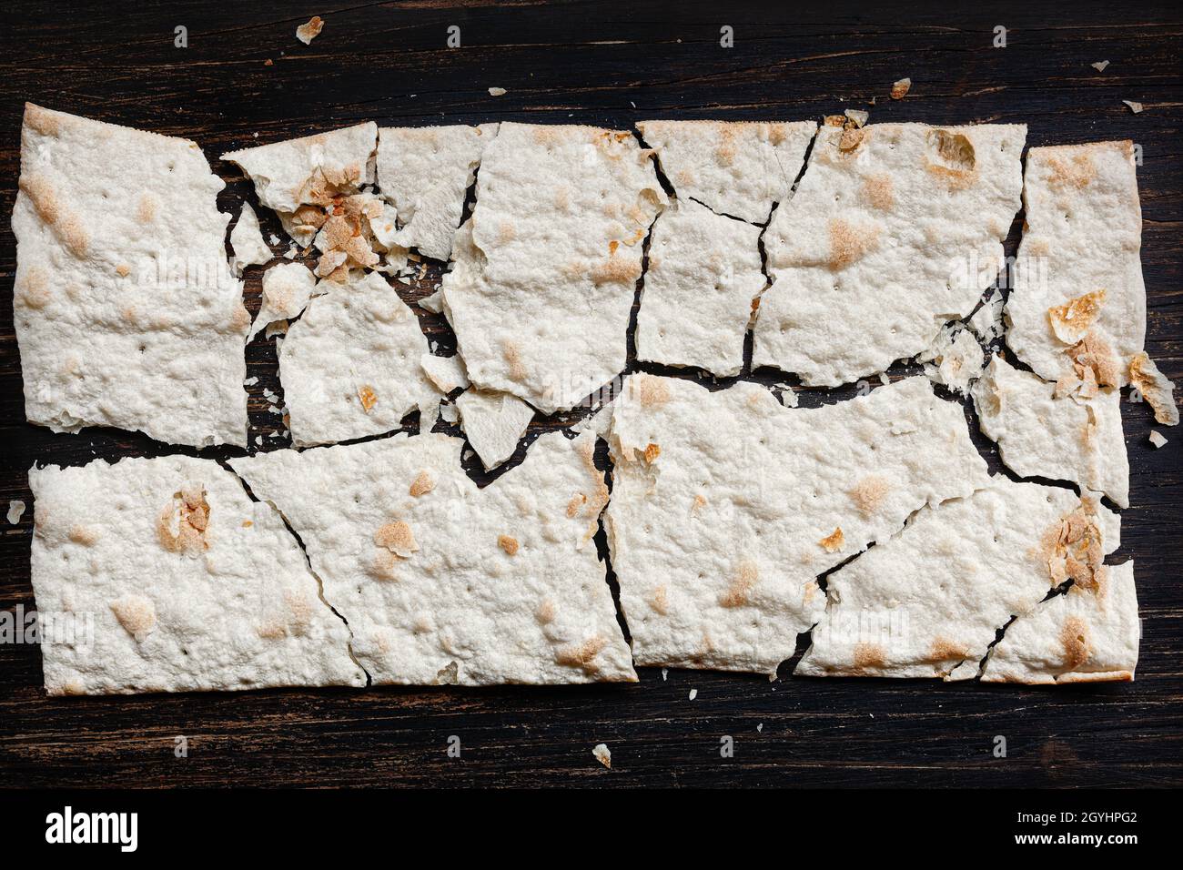 Dry flat bread broken in pieces and divided, with crumbs, on dark ...