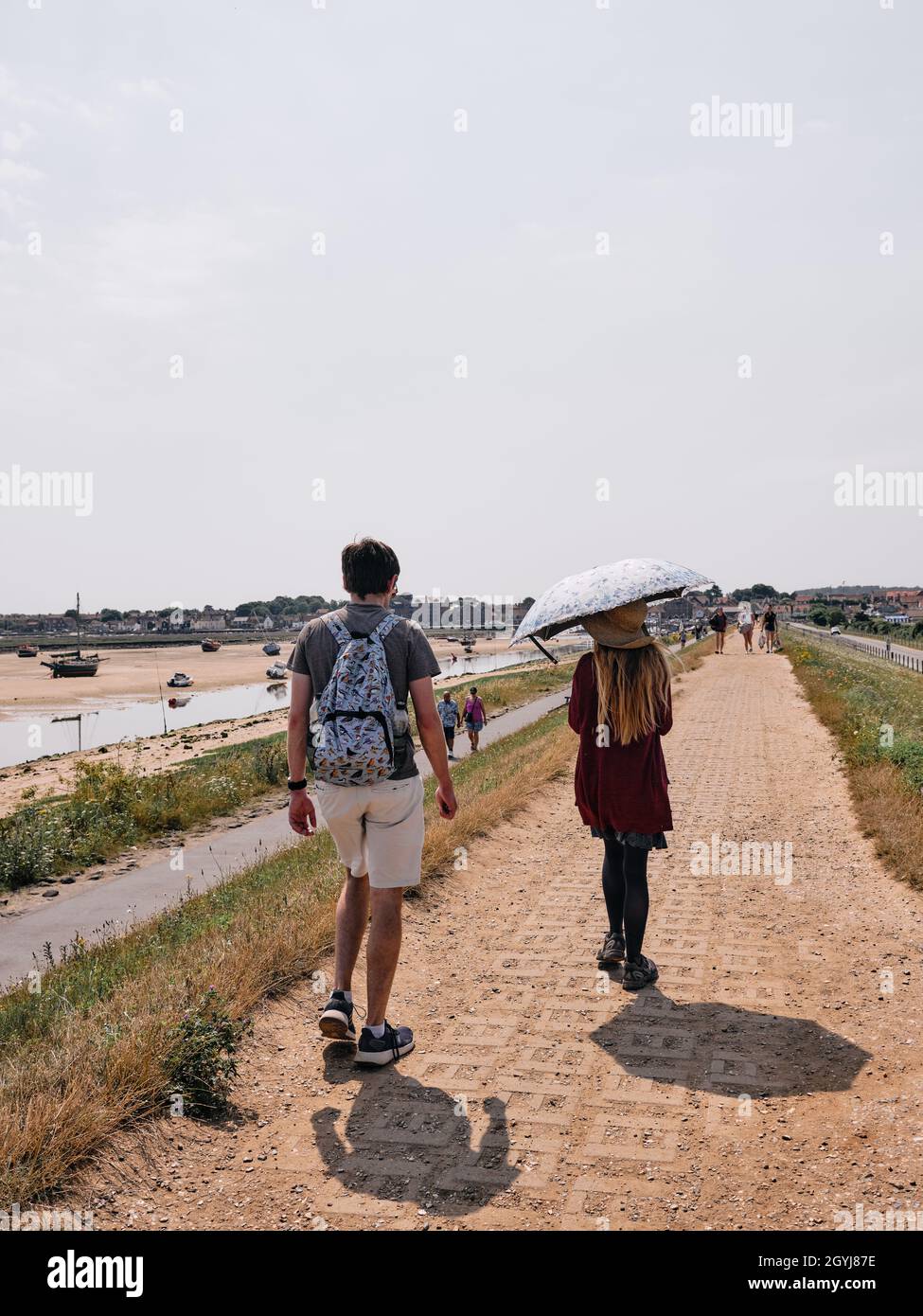 Summer tourists with parasol walking the raised beach footpath in Wells ...