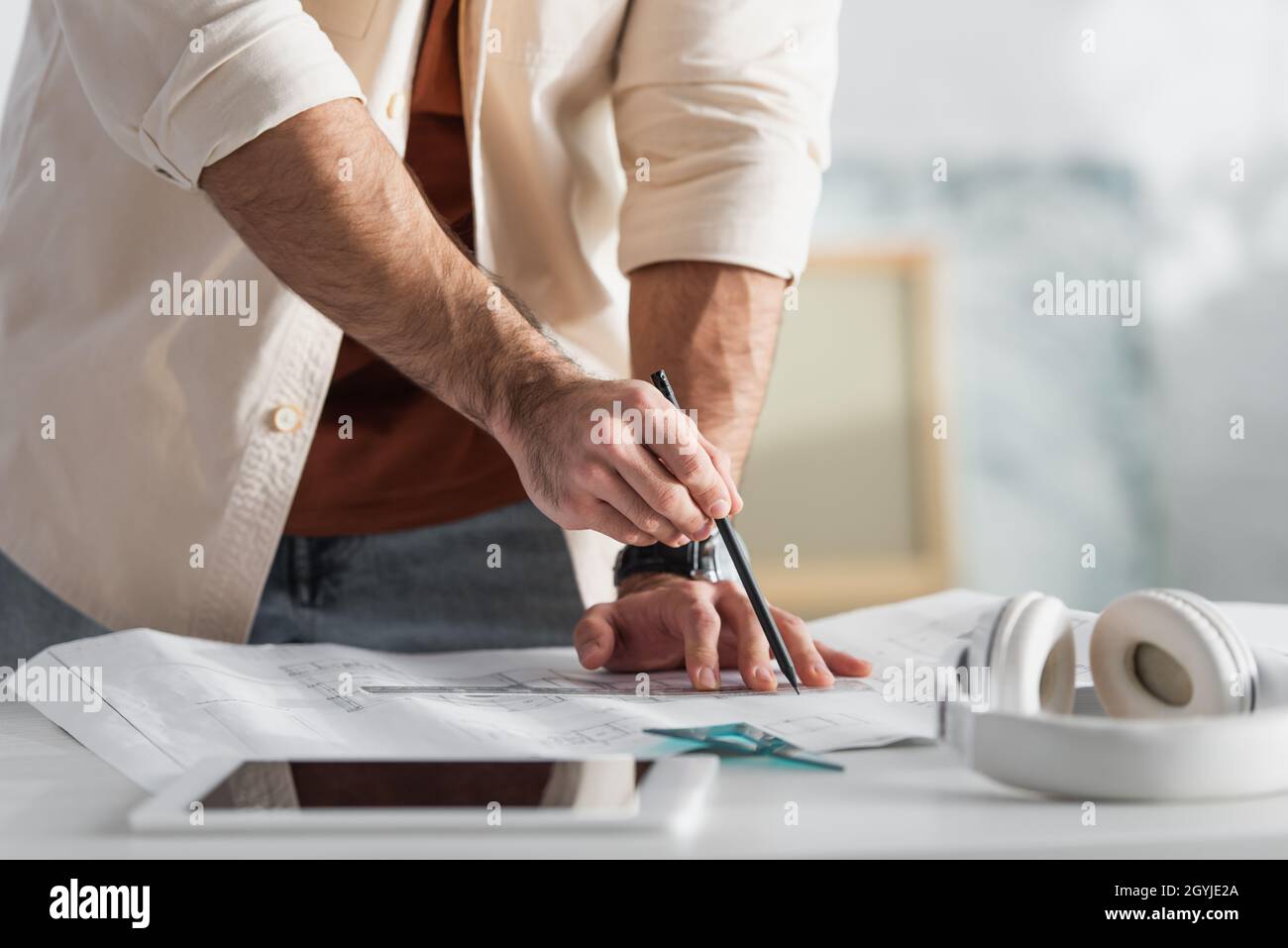 partial view of designer drawing on blueprint near blurred digital ...