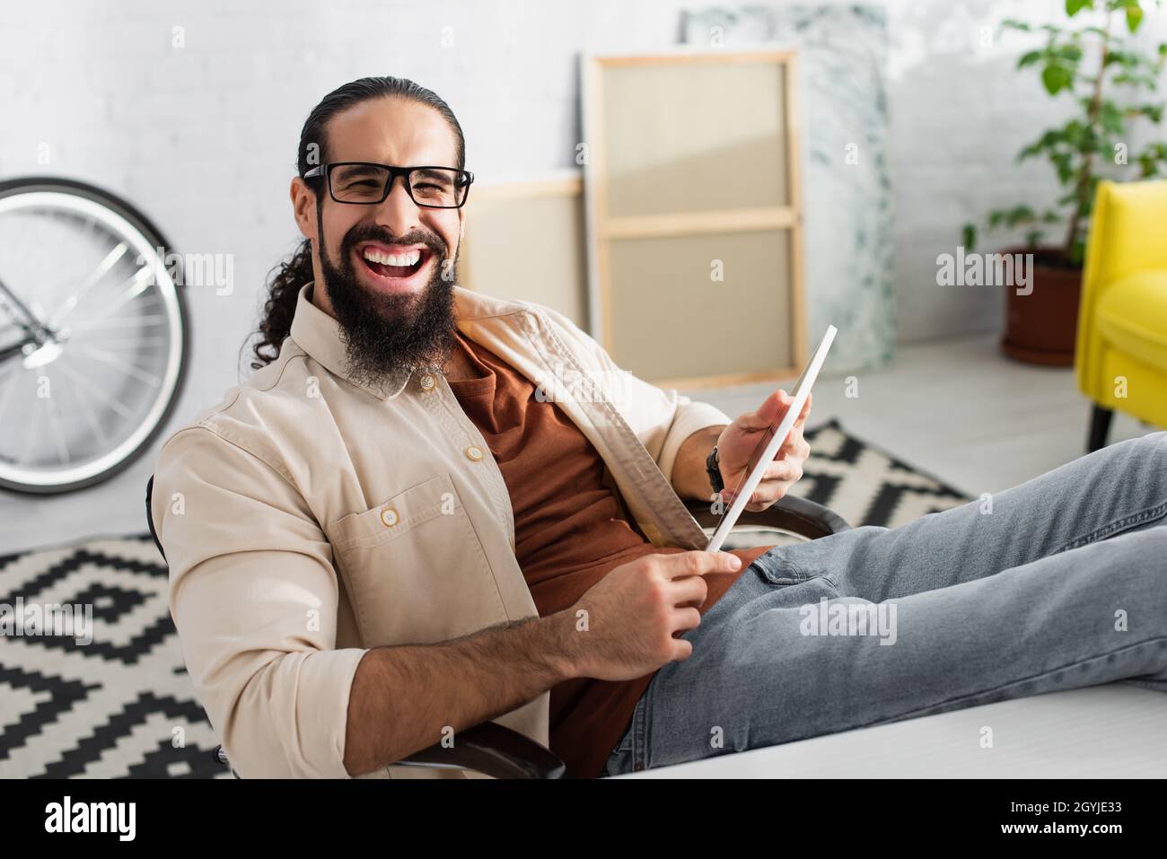 excited hispanic man holding digital tablet and laughing at camera ...