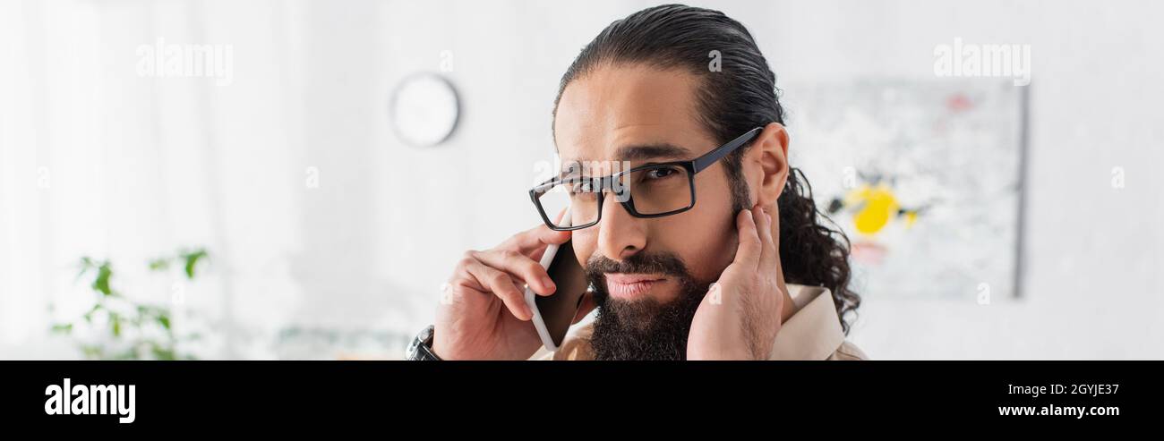 thoughtful latin man in eyeglasses looking at camera while talking on ...