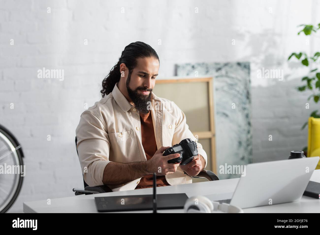 hispanic photographer holding digital camera near blurred laptop and ...