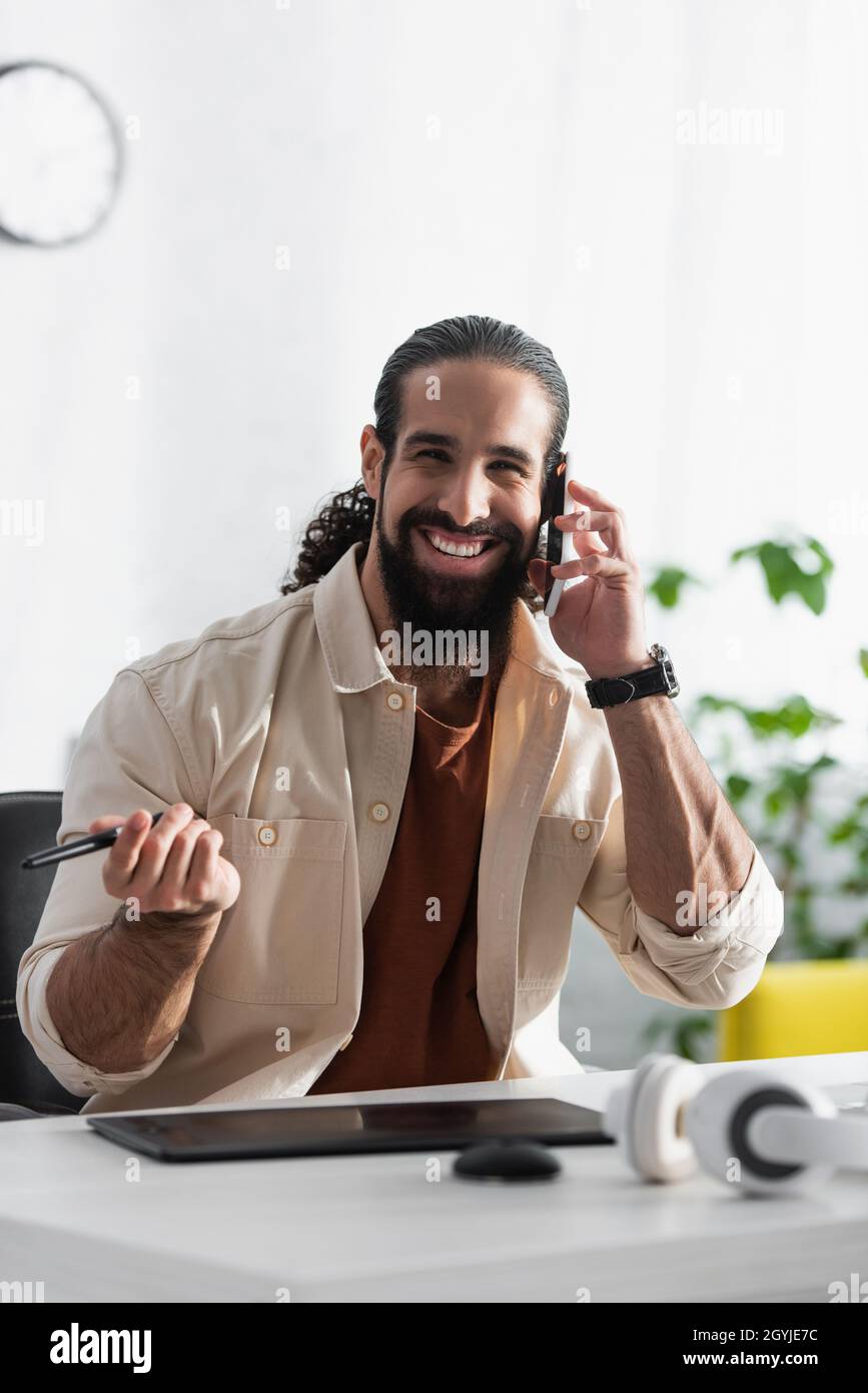 happy designer holding stylus near graphic tablet while talking on ...