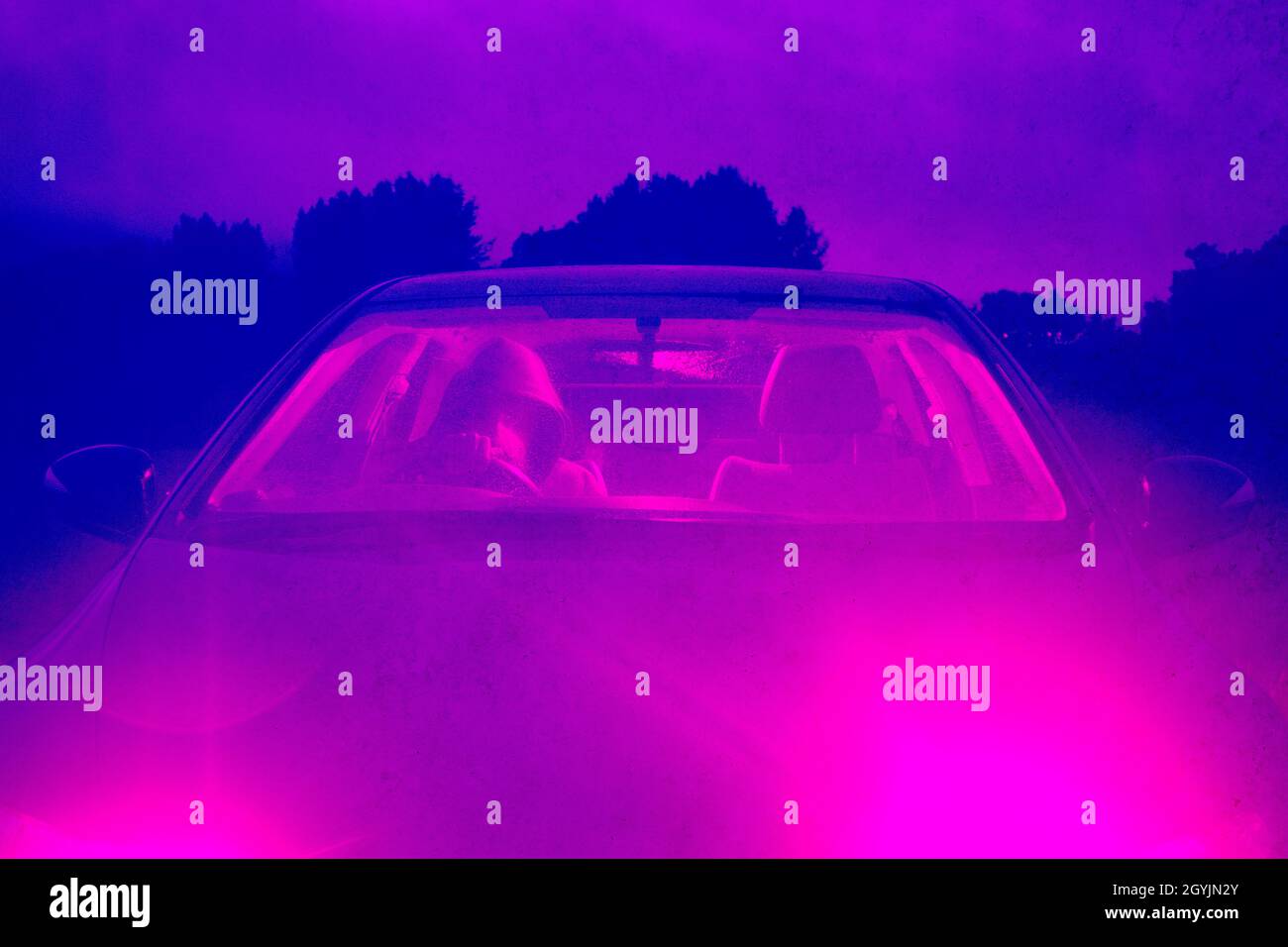 A mysterious hooded figure, sitting in a car at night with headlights ...