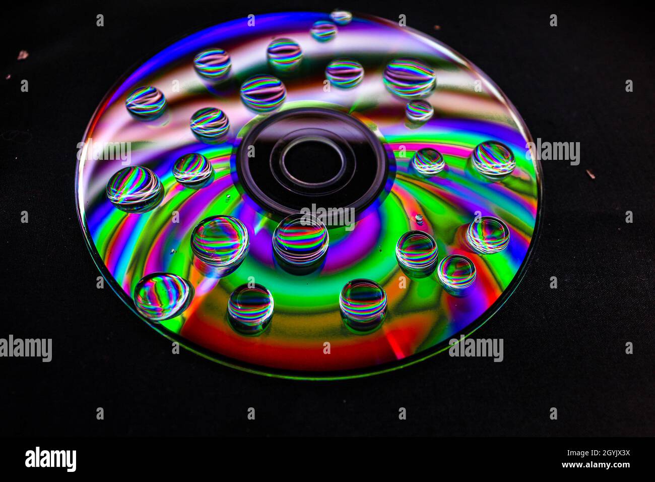 Closeup of a compact disc with rainbow color reflection and water drops ...