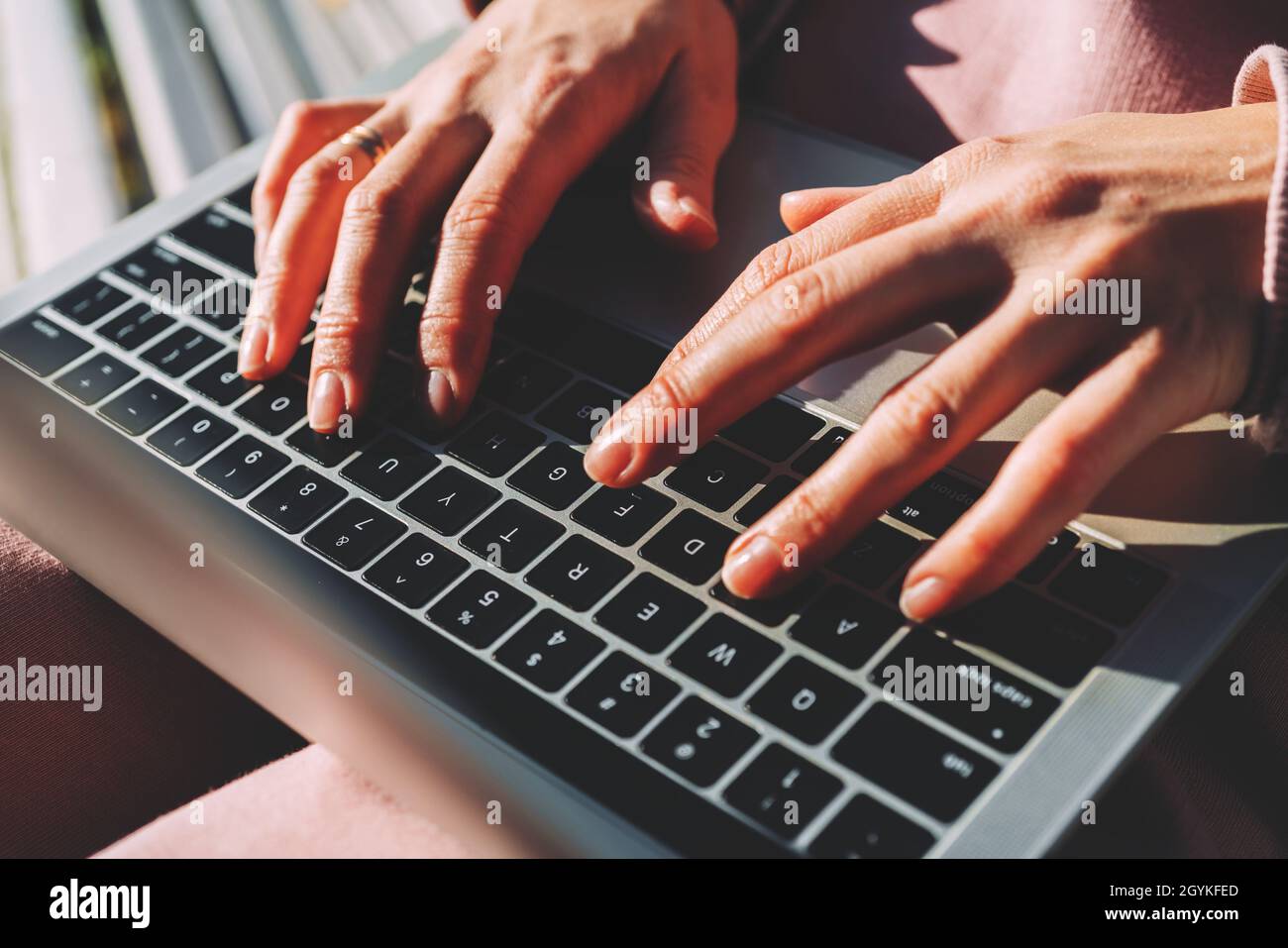 The girl is typing the text behind a laptop while sitting on a bench in ...