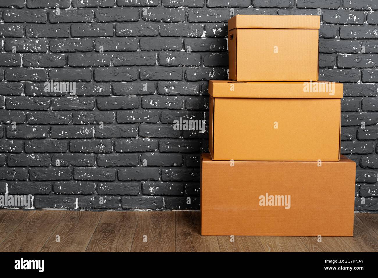 Stack of cardboard boxes in the empty room against black brick wall ...