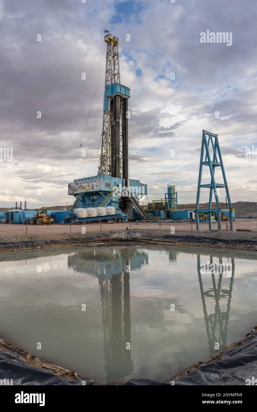 An oil drilling rig is reflected in the water of the reserve pit on a ...