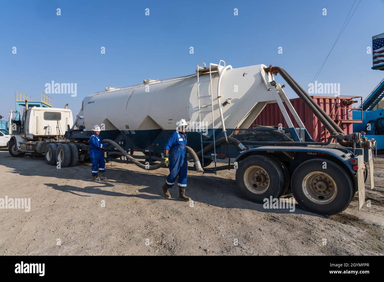 Oilfield workers unload a hose to transfer dry cement from their truck ...