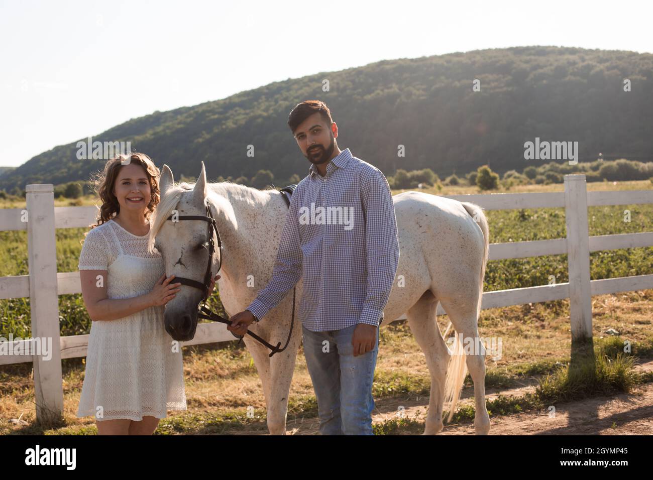 Couple walk at the ranch. The young bearded man leads a white horse ...