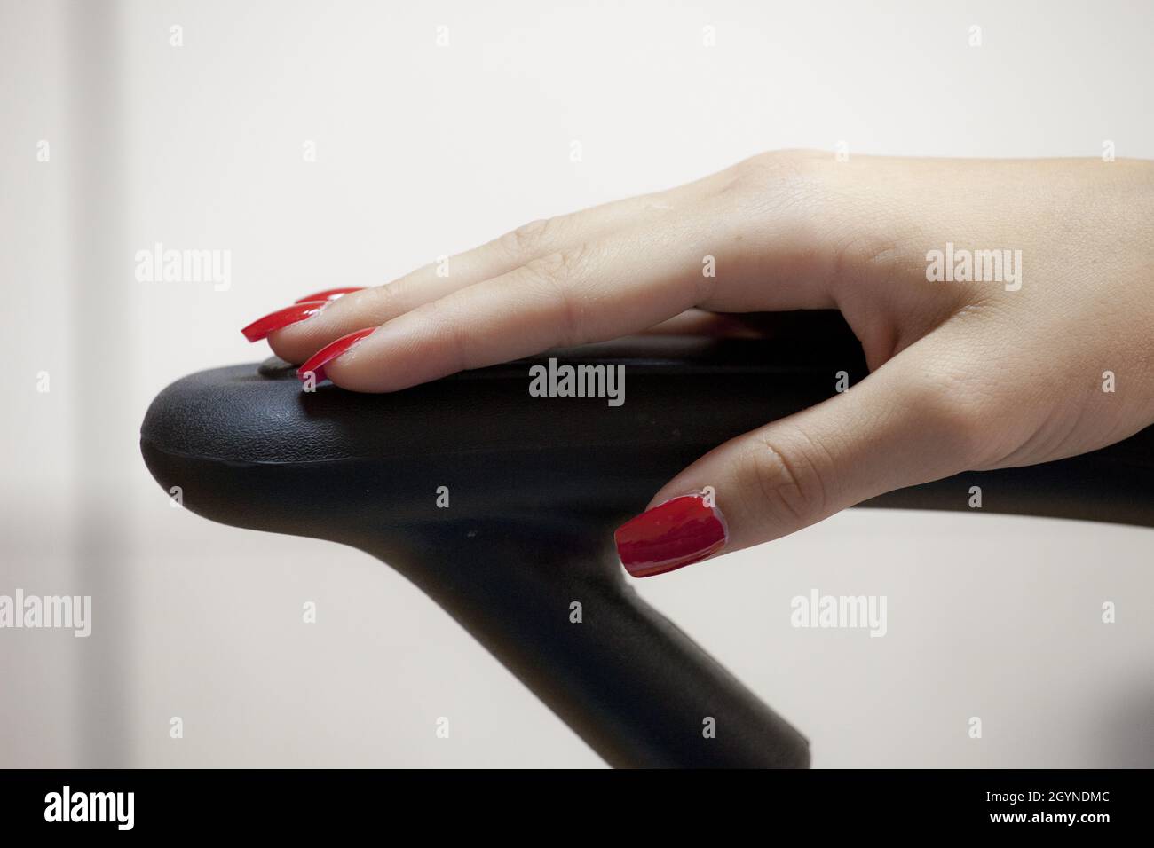 Closeup shot of a hand with red nail polish resting on a black chair ...