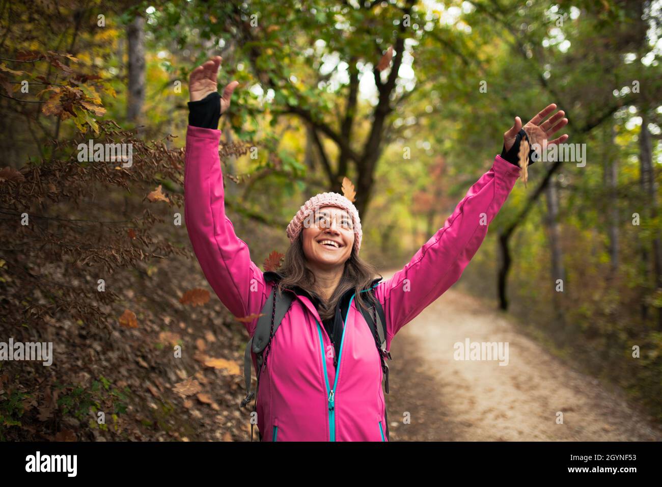 Hiking girl in pink on a trail in the forest. Hands up enjoying the ...