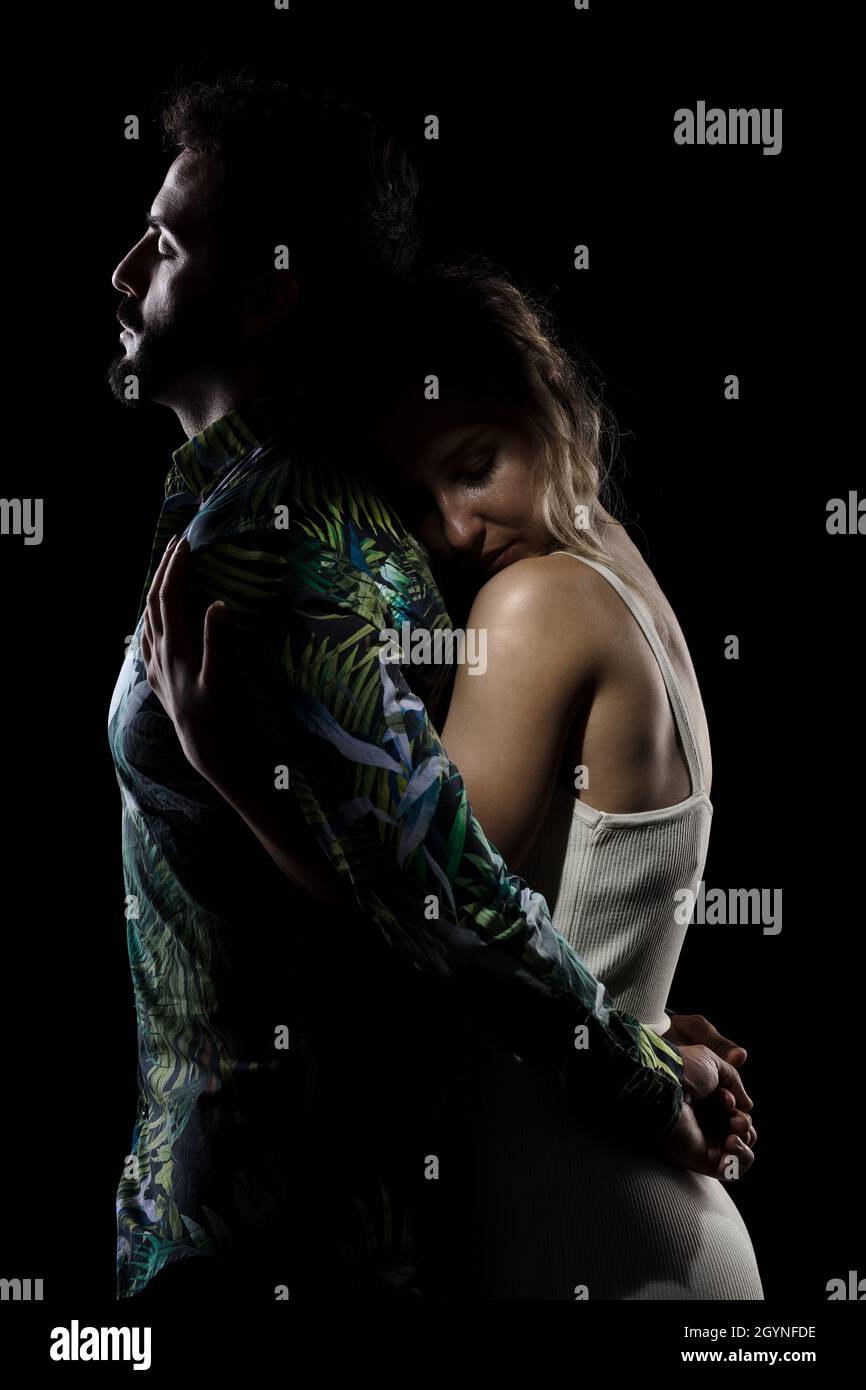 Couple posing on black background. Girl hugging boy in shadow from ...