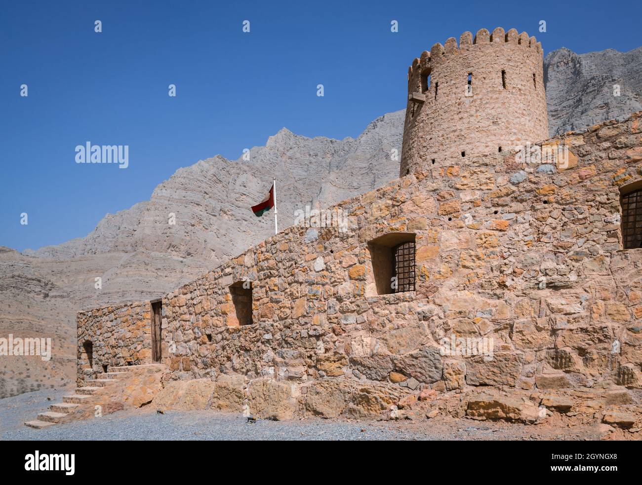 Stone walls of small medieval Arabian fort under tall mountain cliffs ...