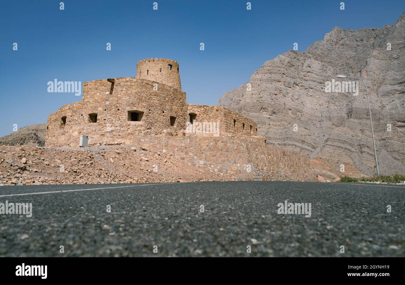 Stone walls of small medieval Arabian fort under tall mountain cliffs ...