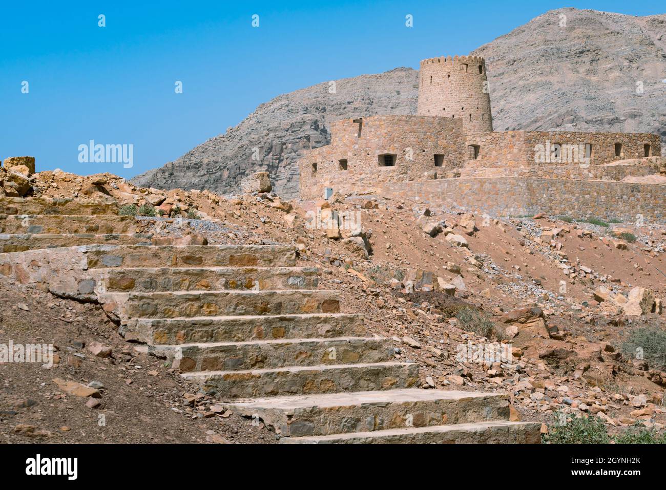 Stone walls of small medieval Arabian fort under tall mountain cliffs ...