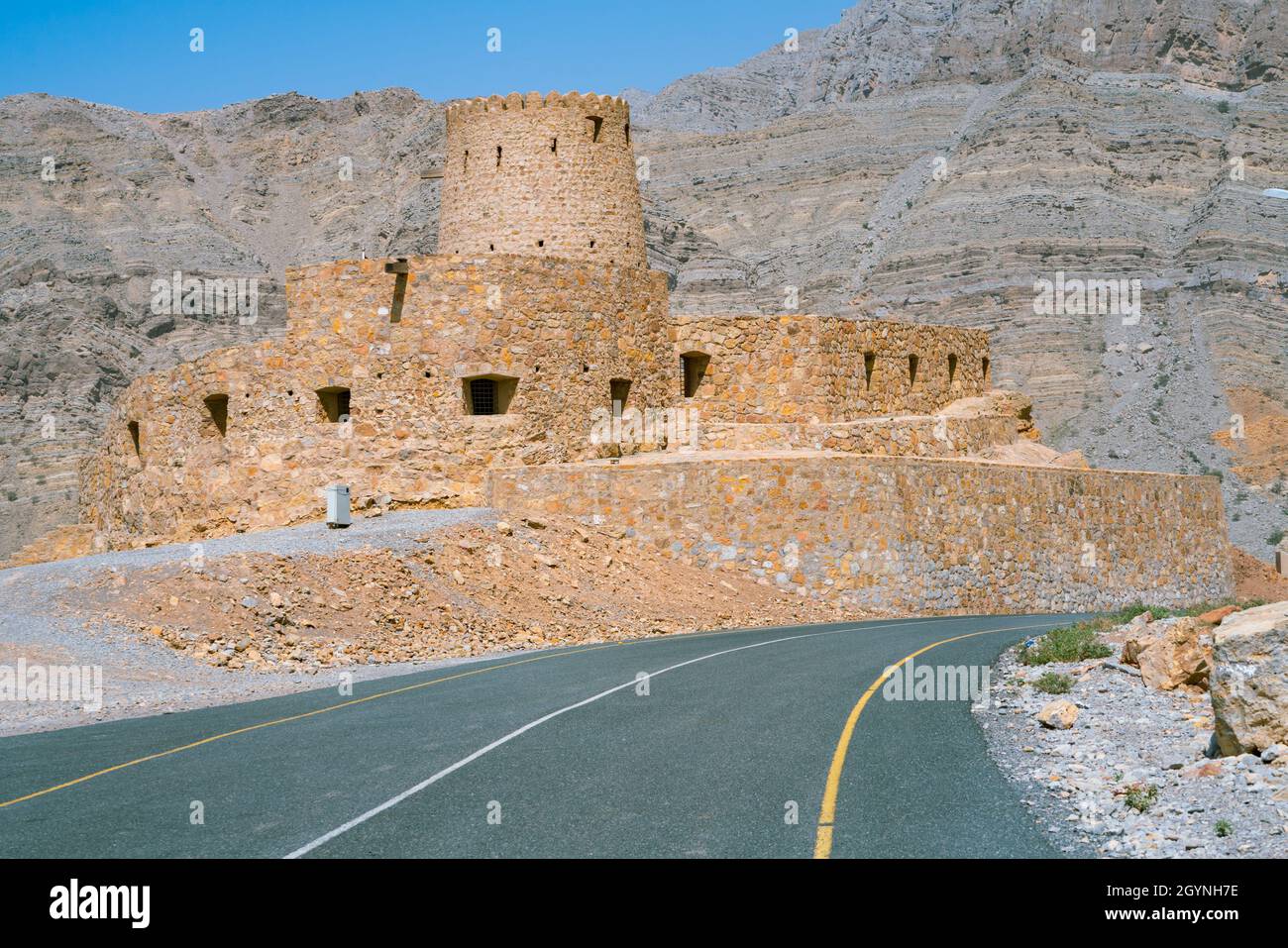 Stone walls of small medieval Arabian fort under tall mountain cliffs ...