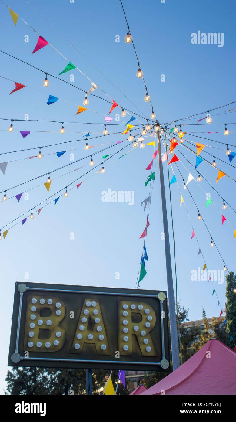 Bar banner with colorful pennants and light bulbs on pole. Outdoors ...