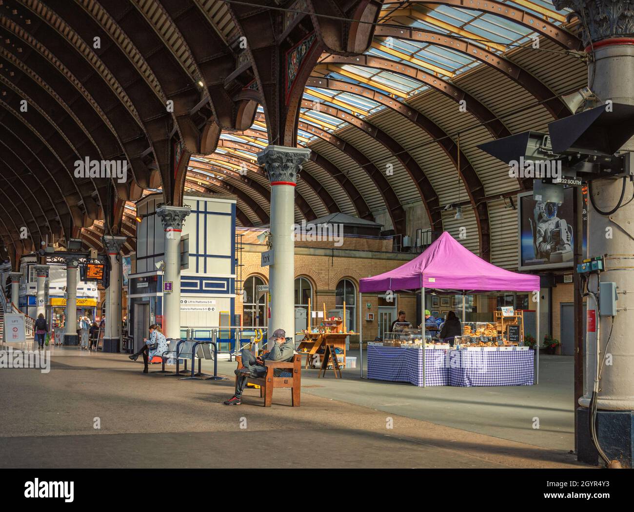 A railway station concourse. An 19th century iron canopy with a skylight curves above the ...