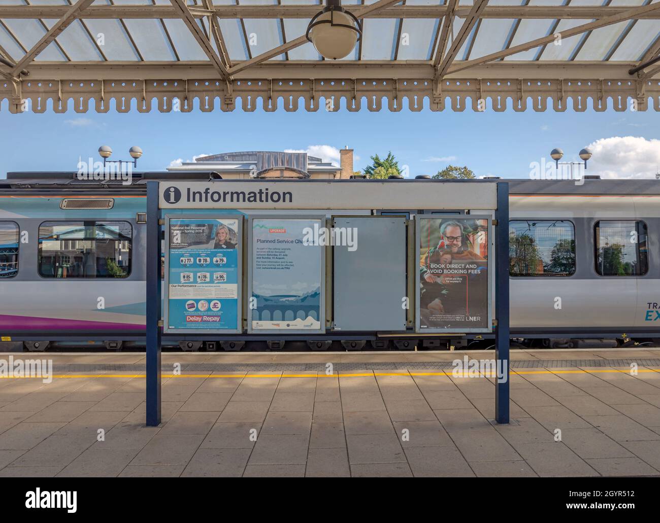 A station platform with a prominent notice board. The carriages of a ...