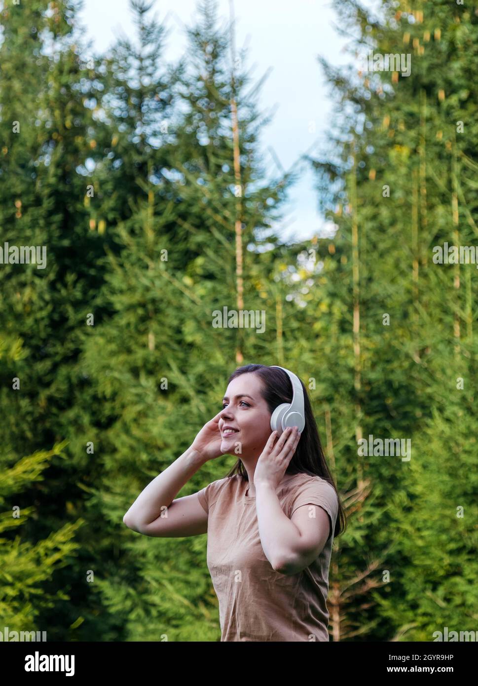 Young woman enjoys listening to music with headphones in forest in ...