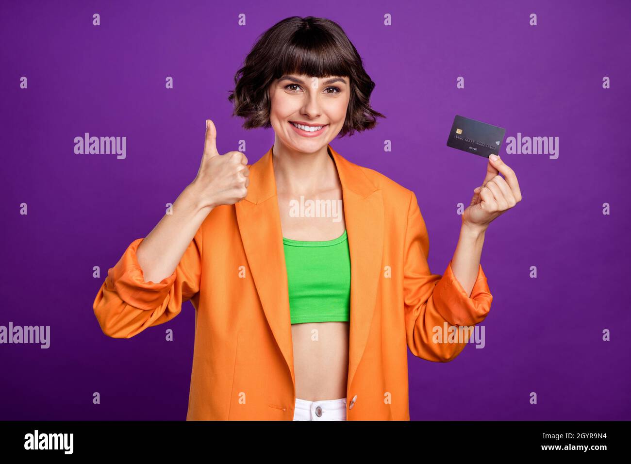 Photo Of Optimistic Young Brunette Lady Hold Card Thumb Up Wear Orange