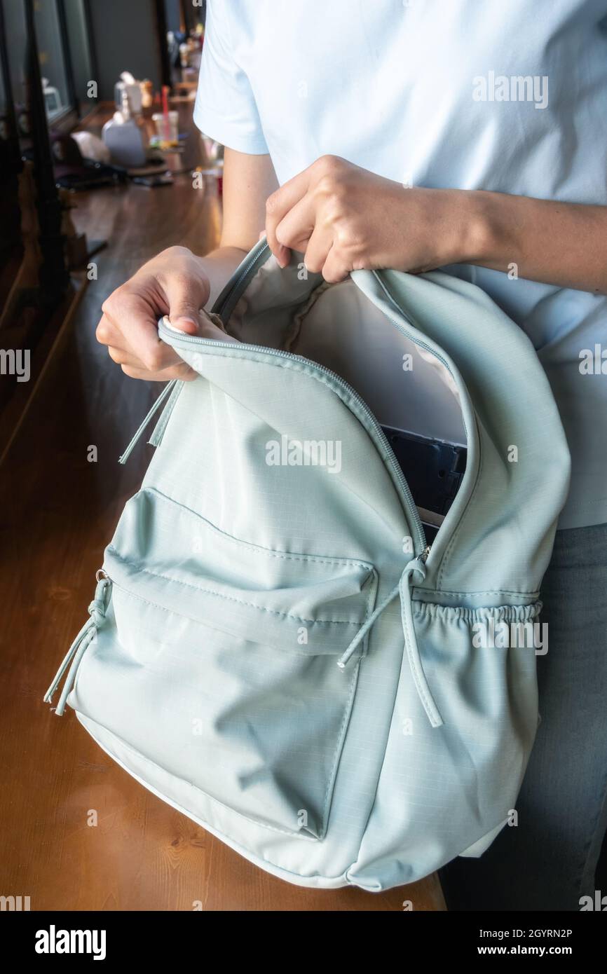 Close-up of the hand of a young female student packing a blue backpack ...