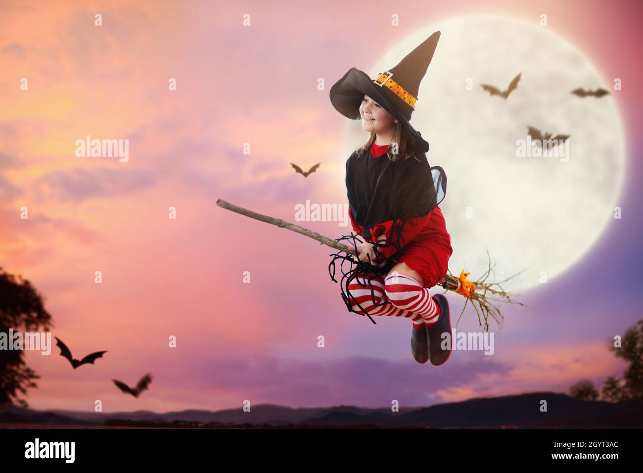 Little witch flying broom on Halloween night. Huge full moon and bats ...