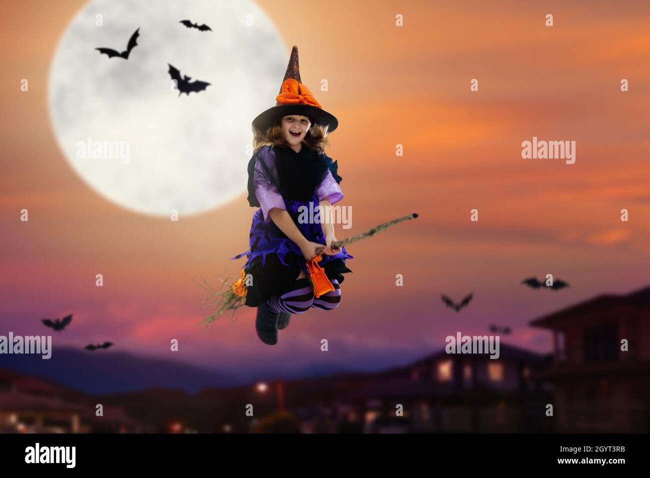 Little witch flying broom on Halloween night. Huge full moon and bats ...