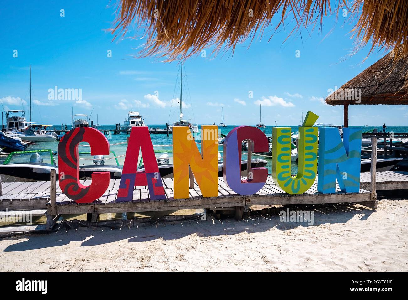 Colorful cancun name sign with pier and moored nautical vessels on sea ...