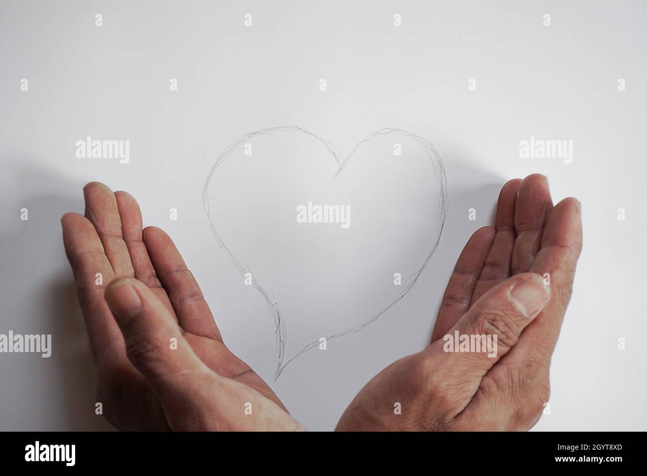 A young man hand caring for a heart shape handwritten from a pencil on ...
