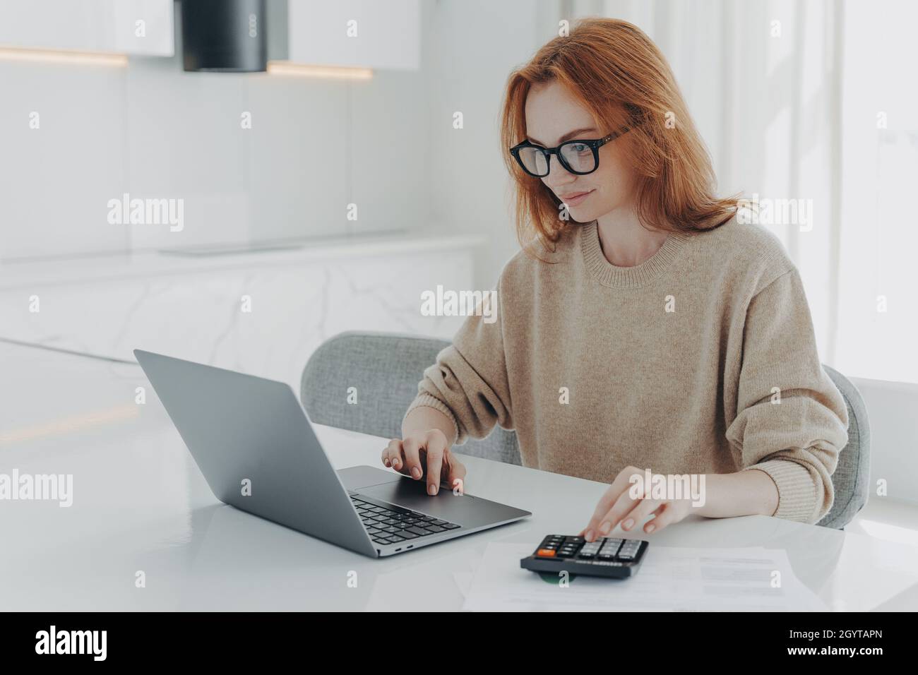Redhead European female accountant analyzes documents uses calculator ...