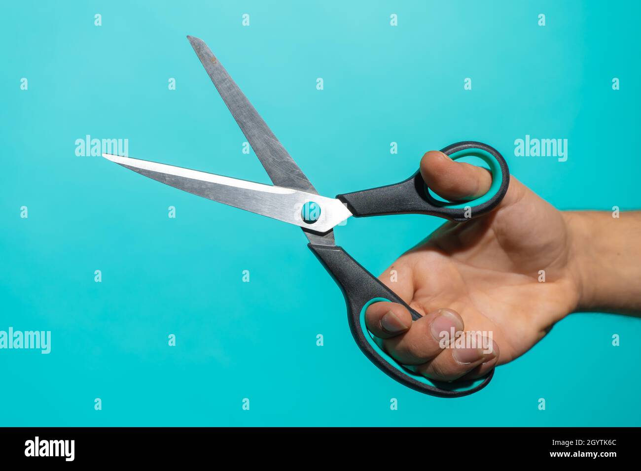 Hand with colorful pair of scissors in front of a blue background with ...