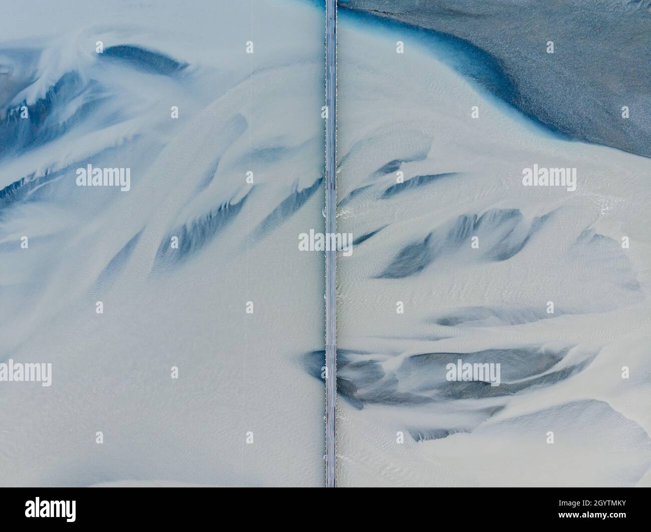 Aerial top view of a large mountain surface covered in snow with a road ...