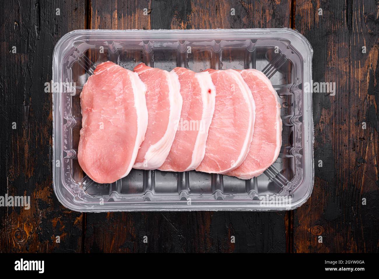 Uncooked pork chop set, in plastic pack container, on old dark wooden ...