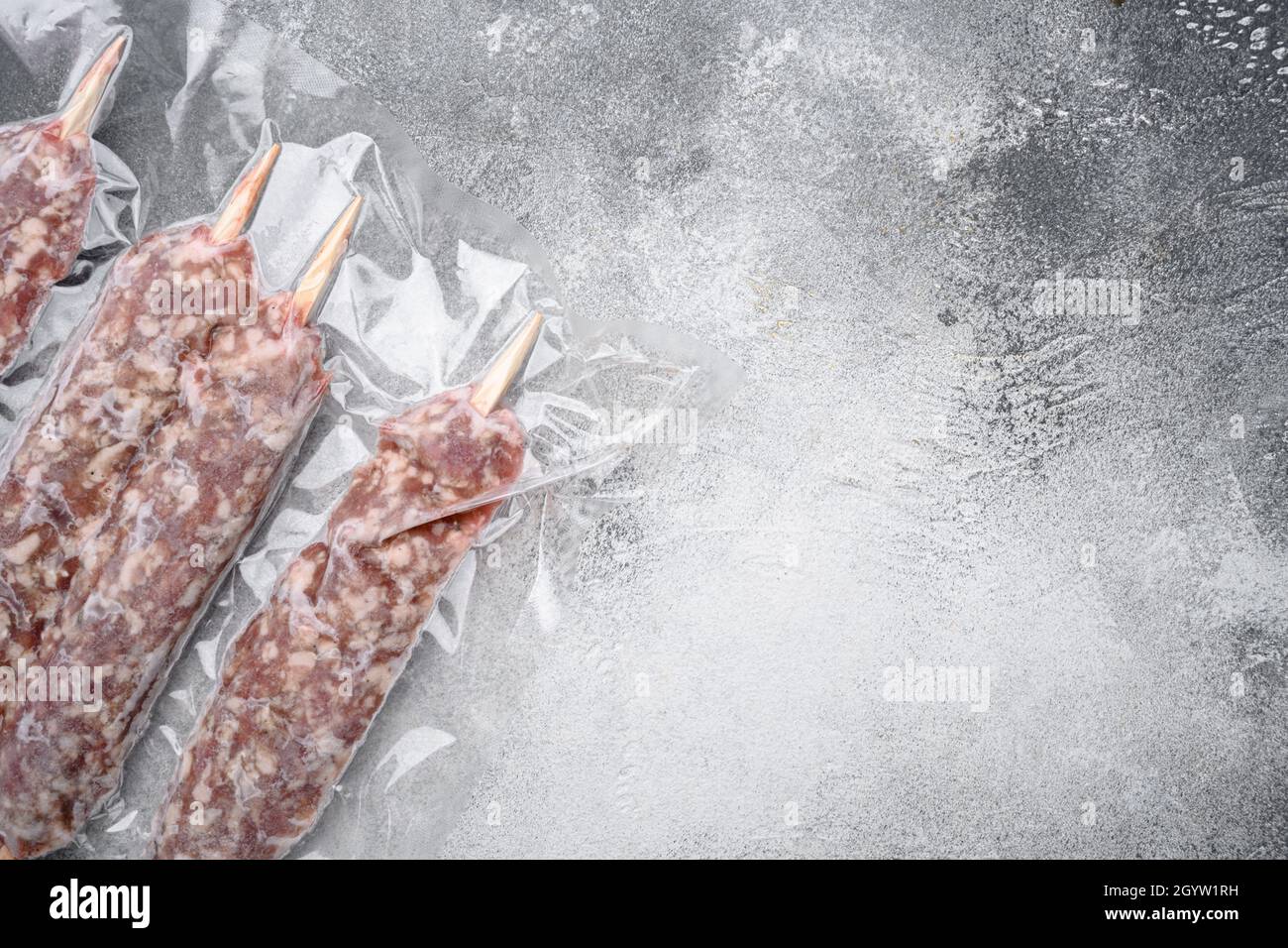 Mutton minced meat on skewers in vacuum pack set, on gray stone table ...