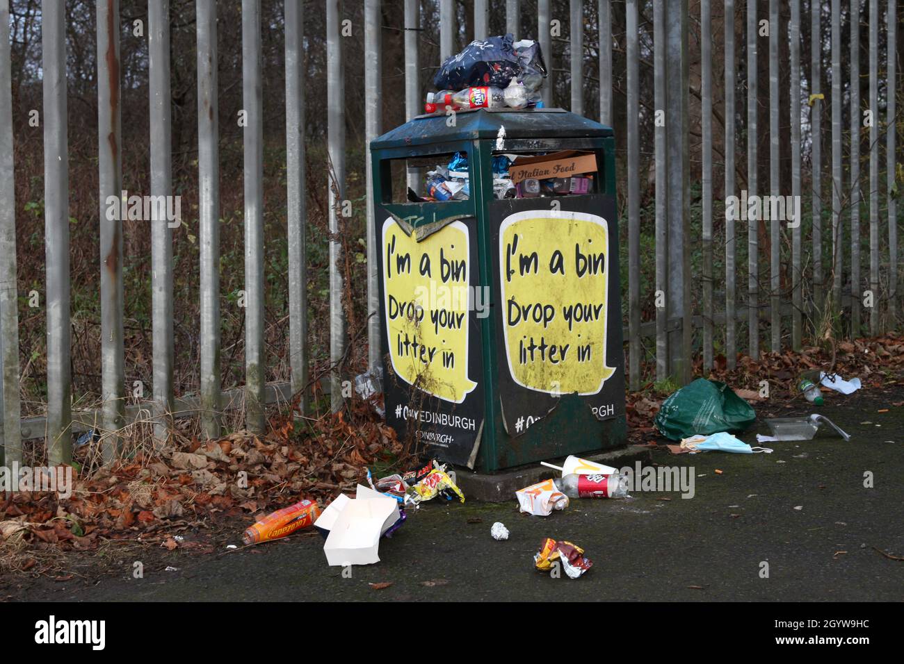Discarded litter lies on the ground surrounding an over filled bin ...