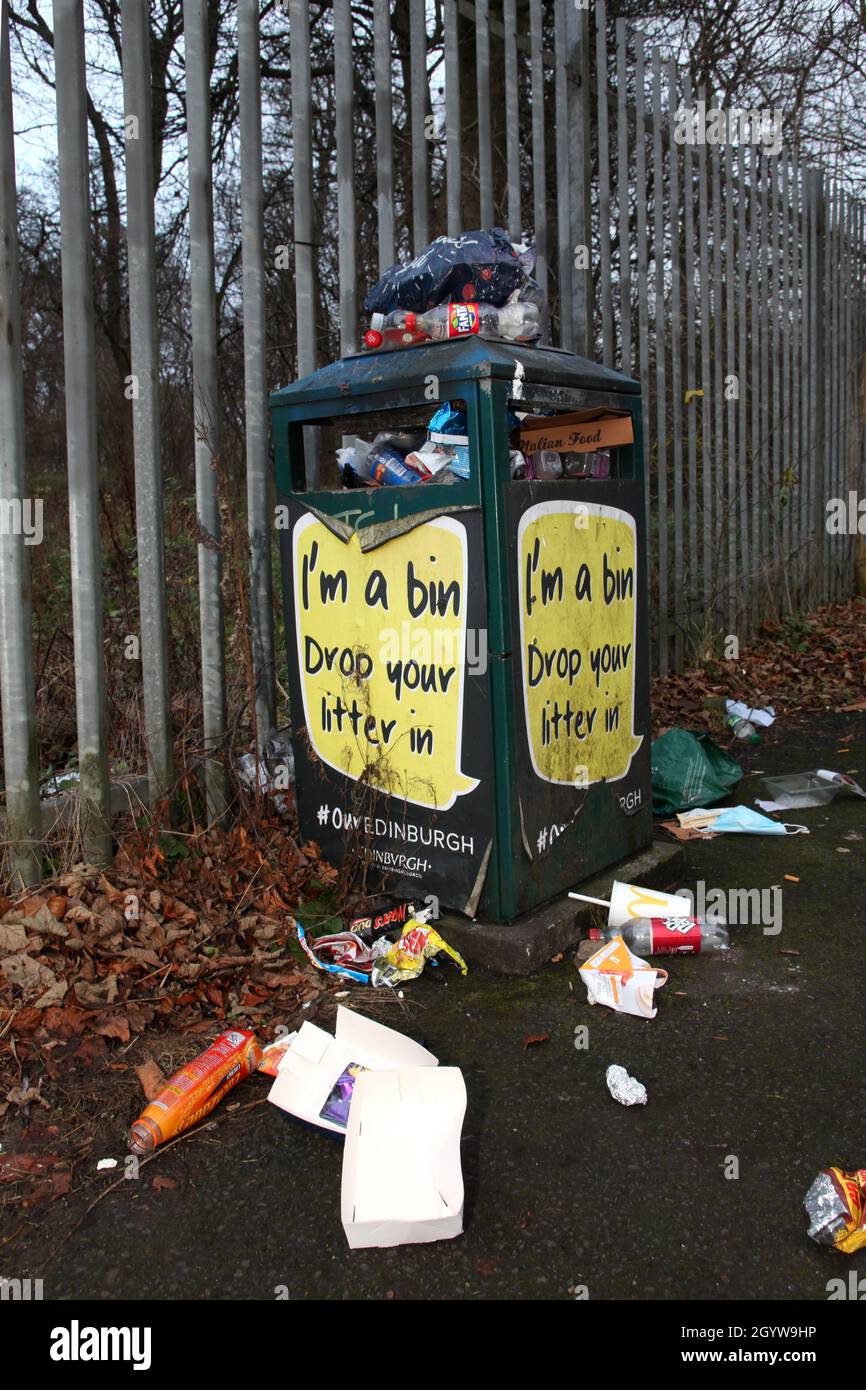 Discarded litter lies on the ground surrounding an over filled bin ...