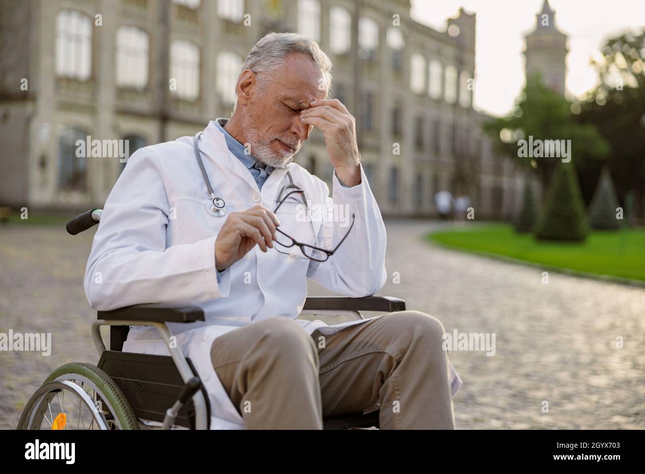 Tired senior handicapped male doctor in wheelchair wearing lab coat ...