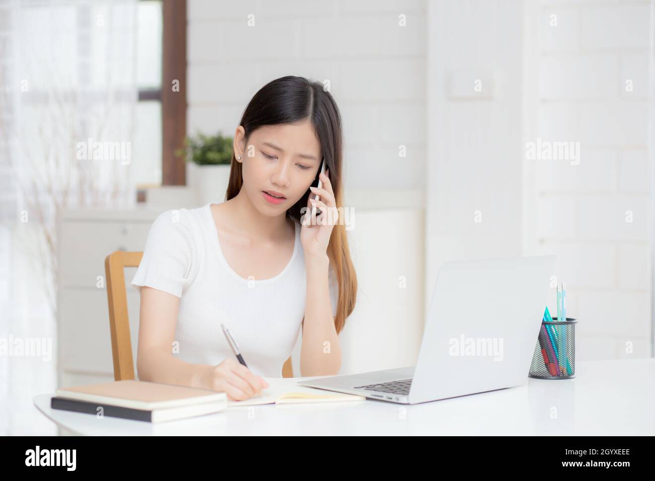 Young asian woman working on laptop computer and talking smartphone ...