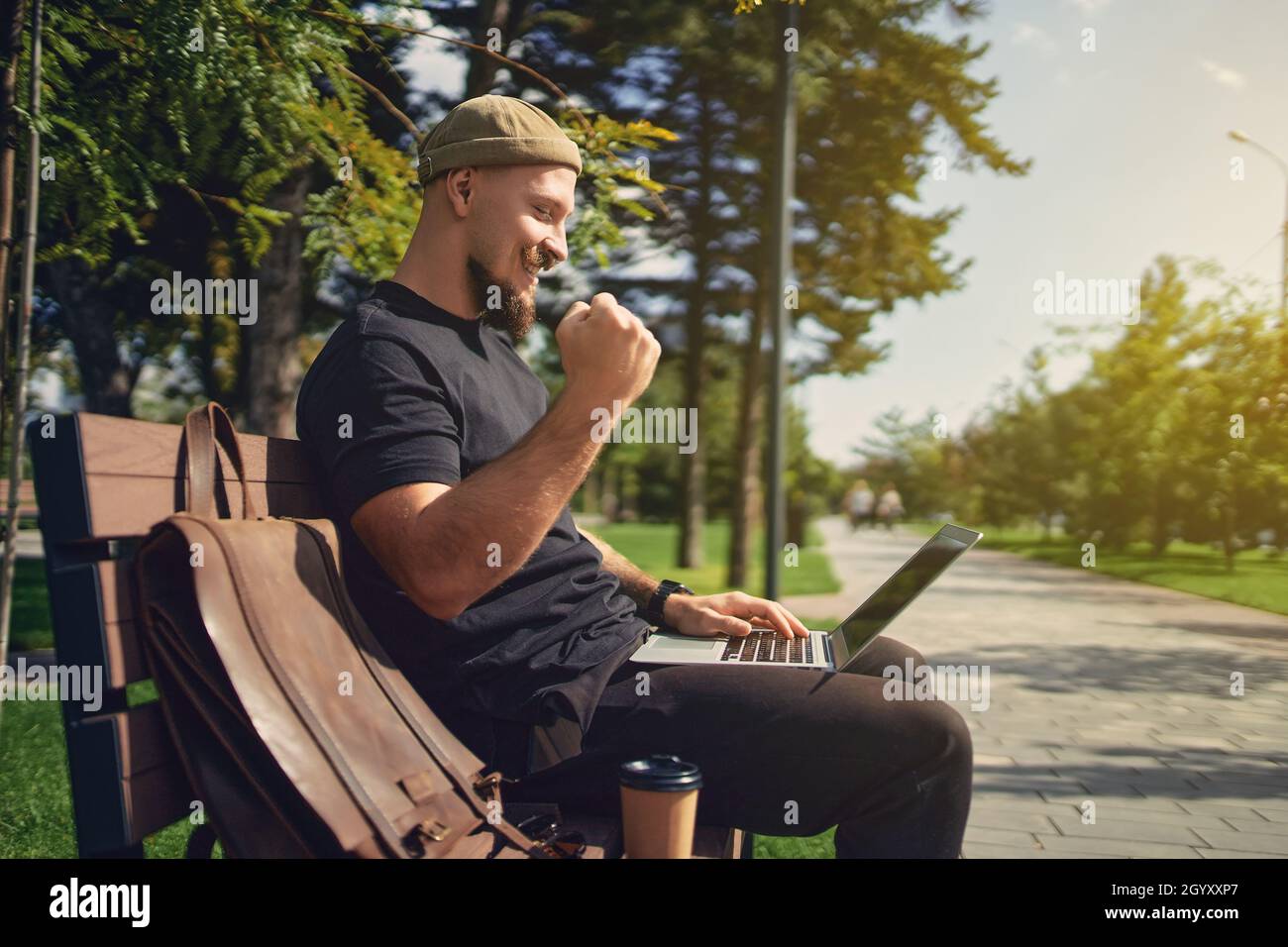 happy victorious millennial sit on the bench outdoor while look at ...