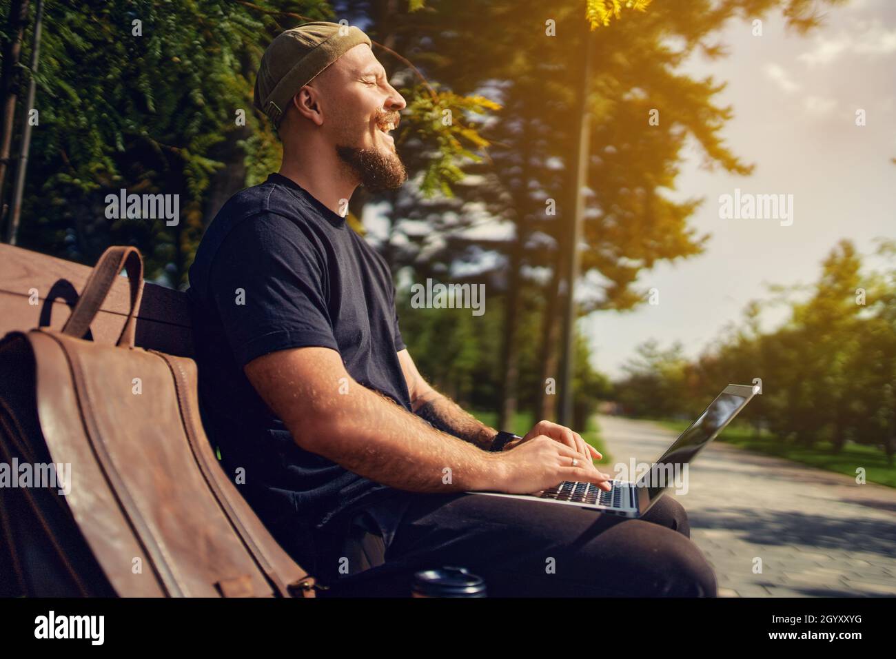 Outdoor photo of laughing millennial sitting on a bench while working ...