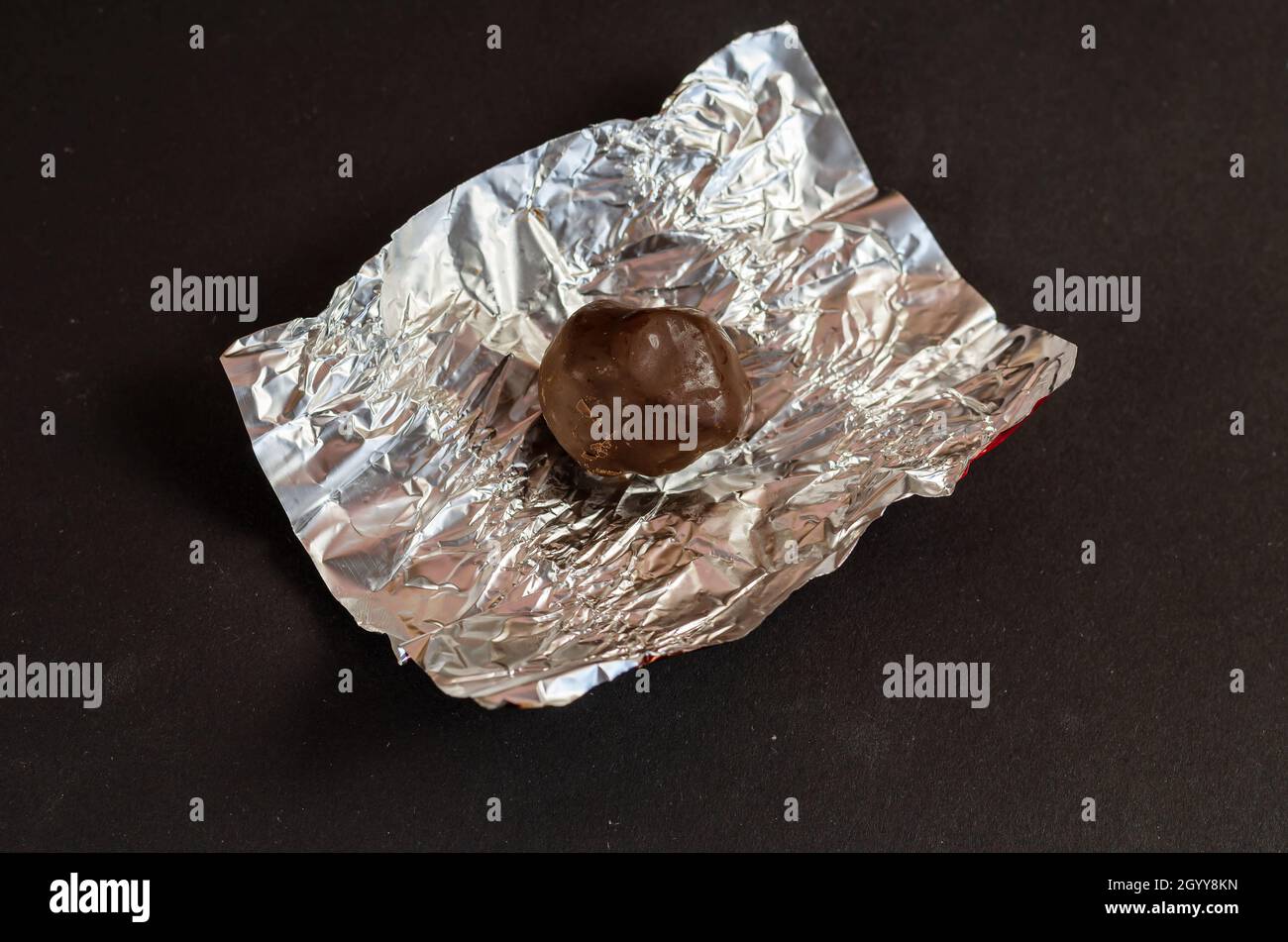 A round chocolate candy in an unwrapped silver wrapper. Crumpled foil ...