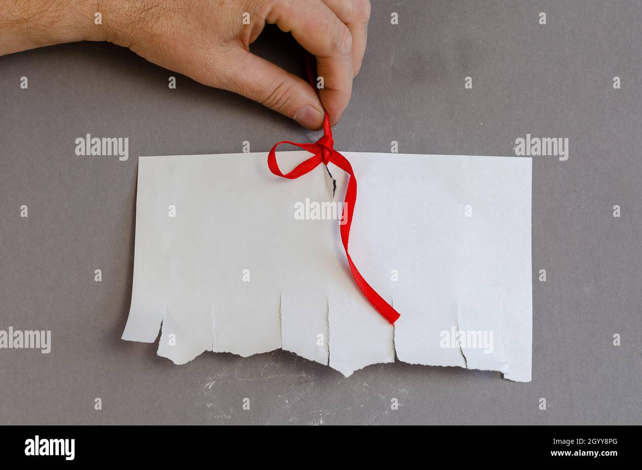 White sheet of paper with tear-off pieces and red ribbon against a gray ...