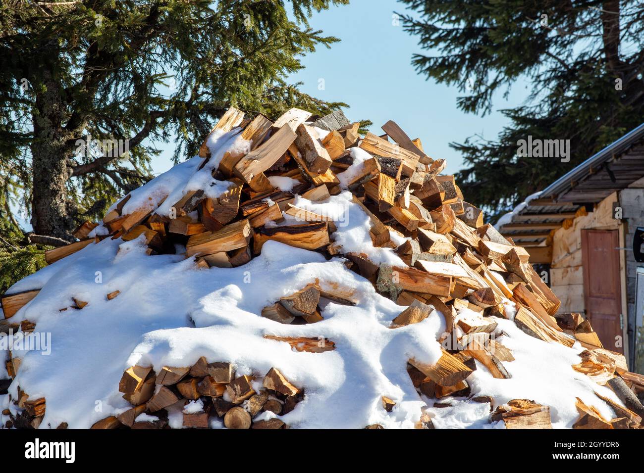 Log pile covered with snow behind village cottage in mountains Stock ...