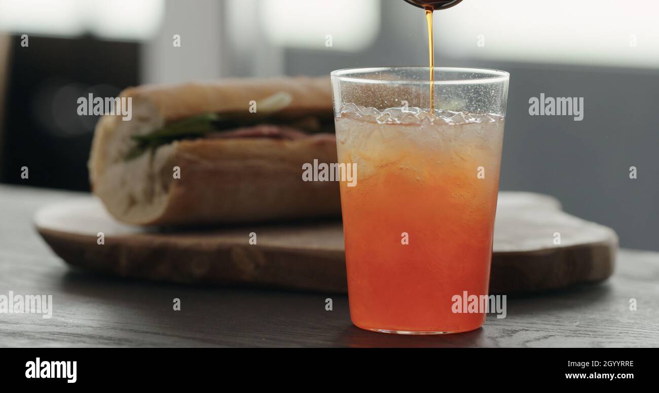 pour syrup in lemonade over crushed ice in tumbler glass on oak table ...