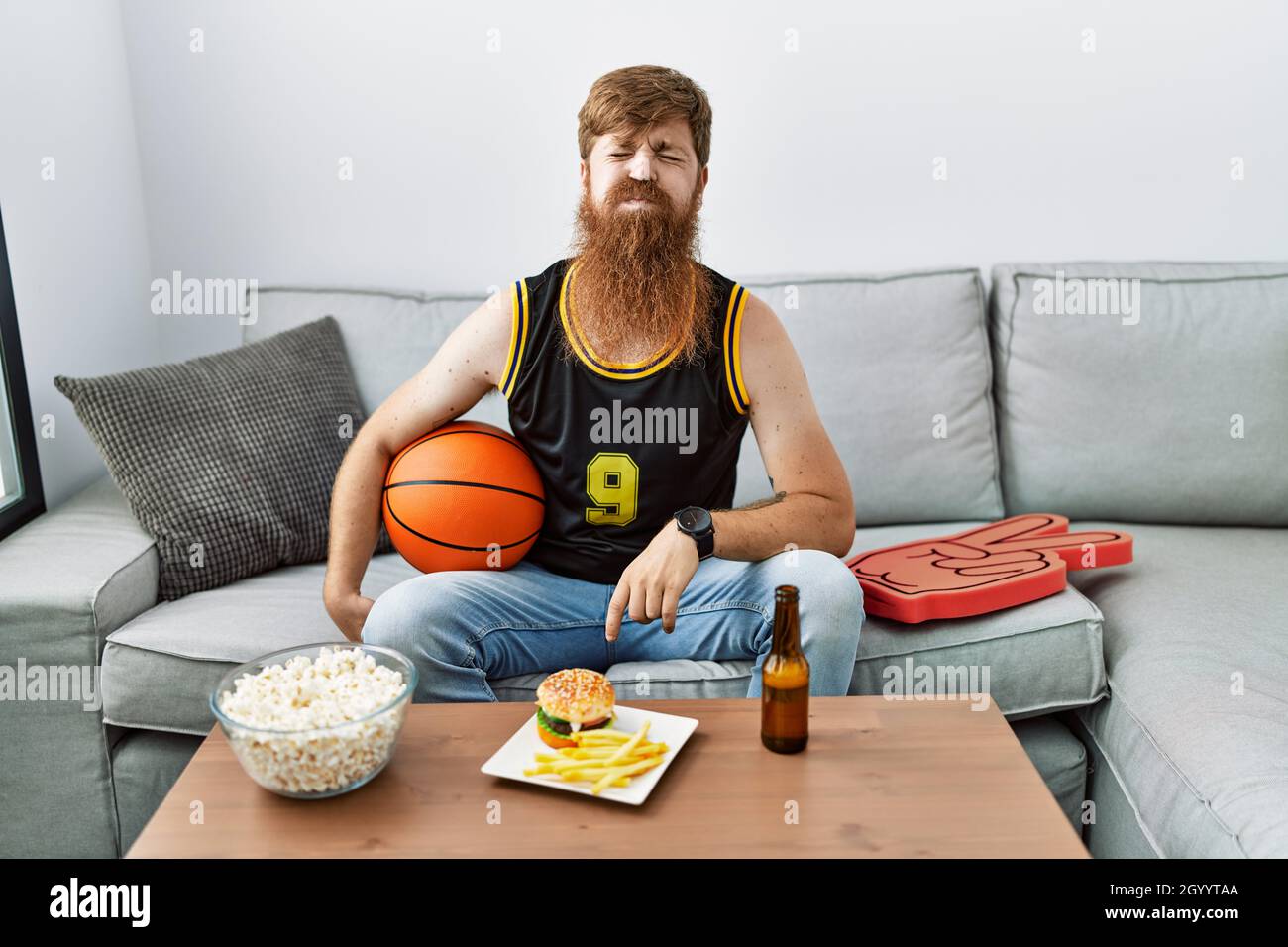 Caucasian man with long beard holding basketball ball cheering tv game ...