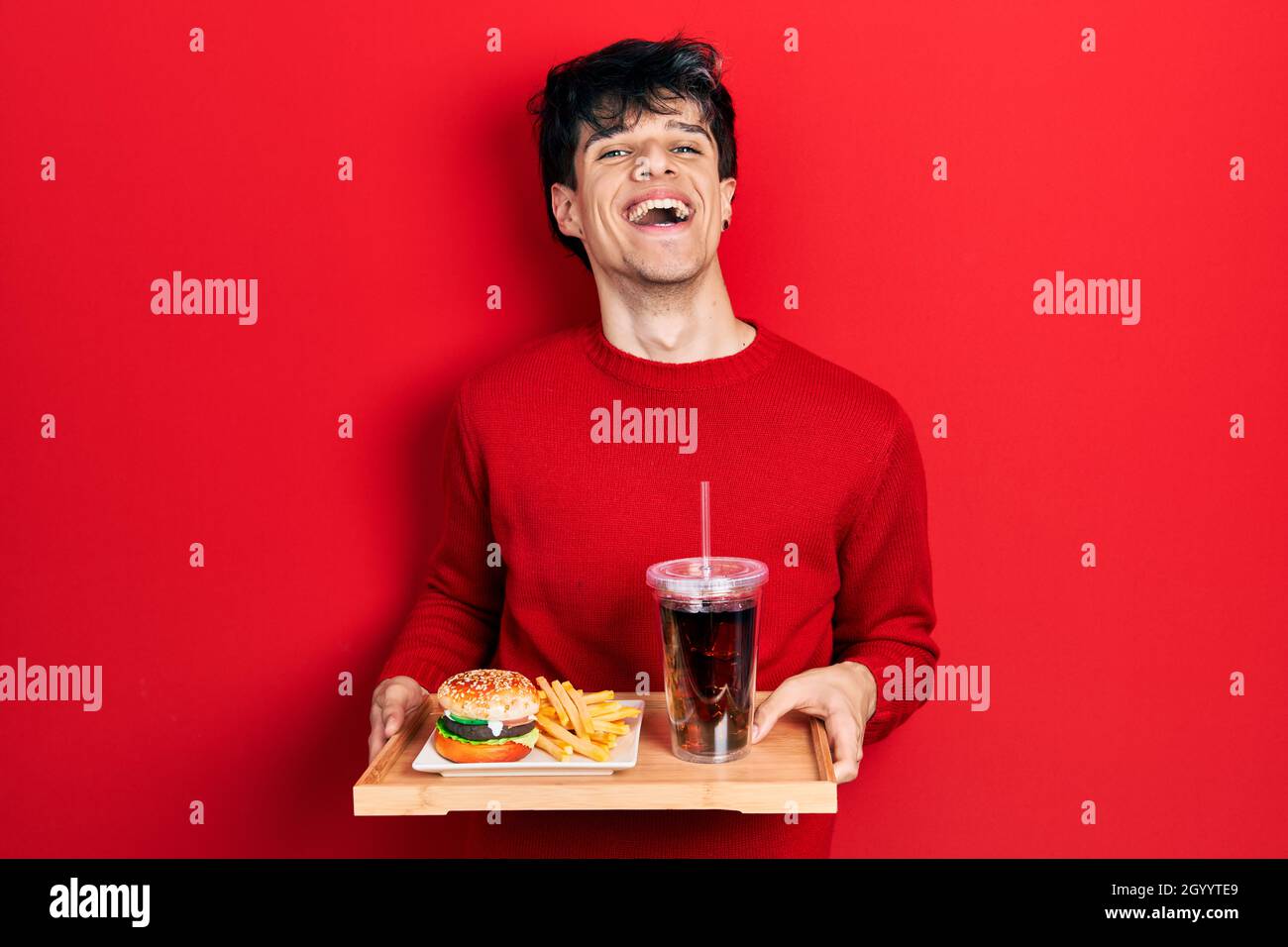 Handsome hipster young man eating a tasty classic burger with fries and ...